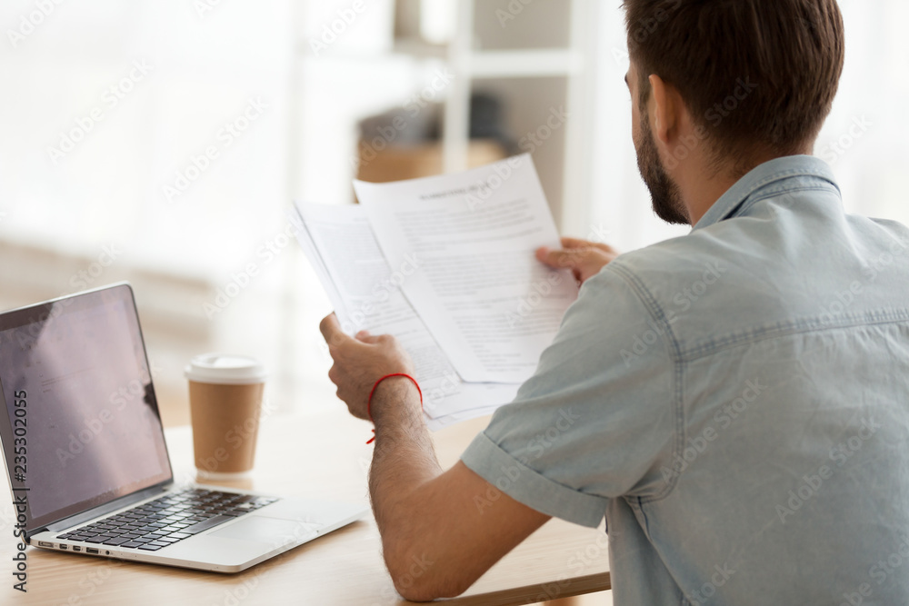Back view of focused man sitting at office table working at laptop ...