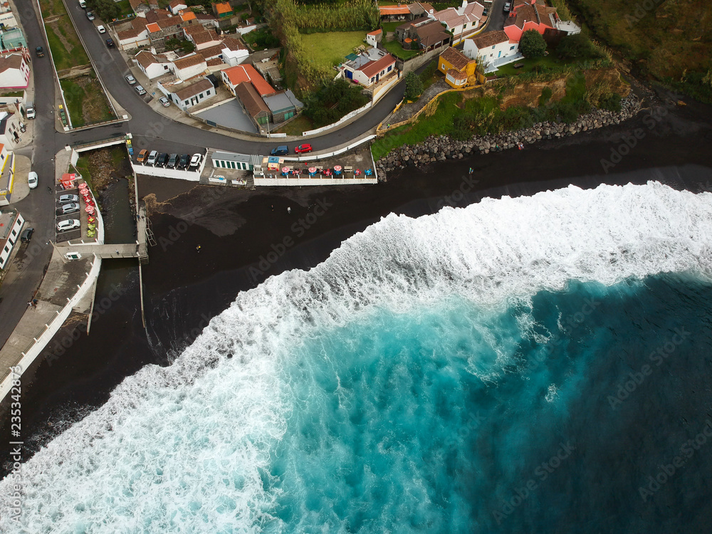 Aerial top view of sea waves hitting a beach with black volcanic sand ...