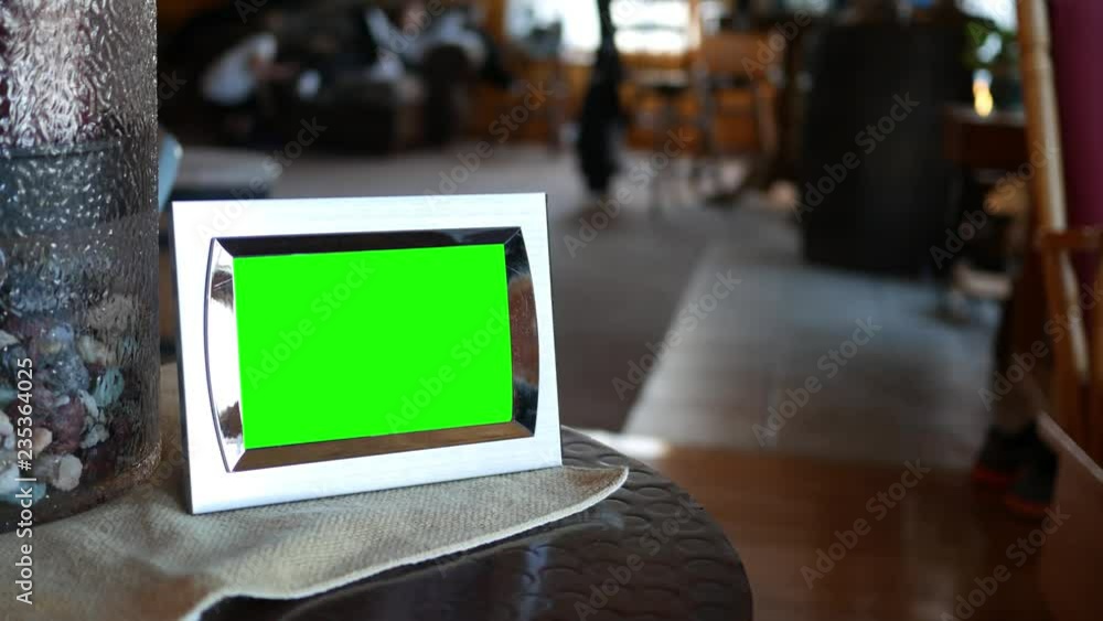 A green screen picture frame sitting on an end table with blurry people ...