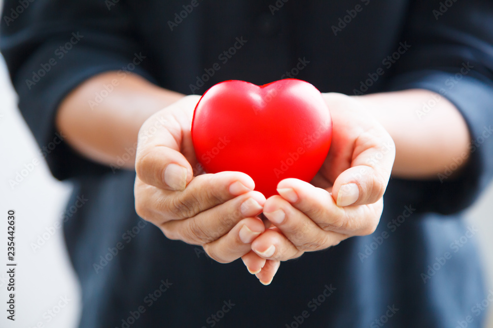 red heart in female's both hands in black suit background, represents ...