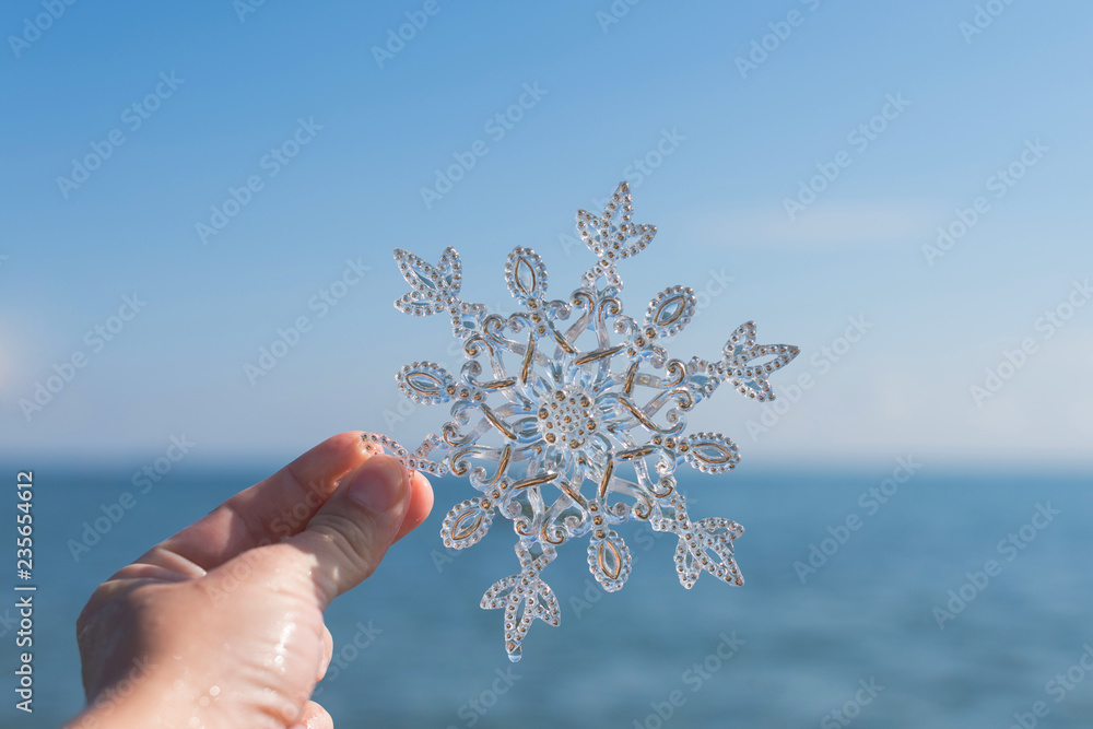 Female hand with sparkling huge snowflake on the sea background ...