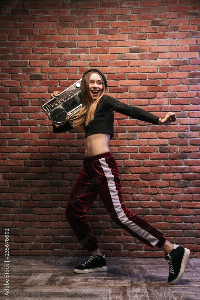 Full length image of subcultural woman 20s, standing against brick wall ...