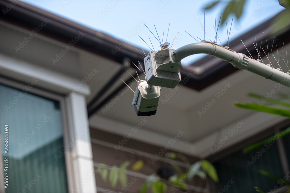 A cantilevered modern white security CCTV camera with pigeon spikes on ...