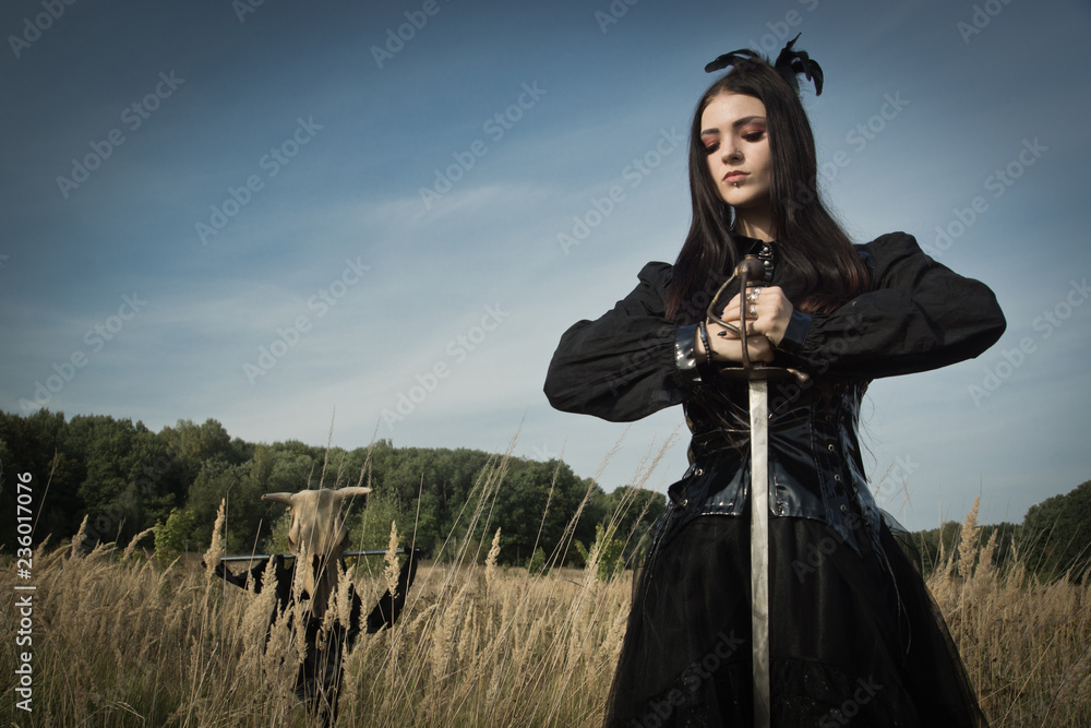Gothic girl with a sword in her hands next to the skull of a cow on a ...