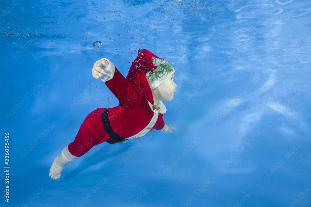 Little baby boy dressed as Santa swim underwater. Baby swimming ...