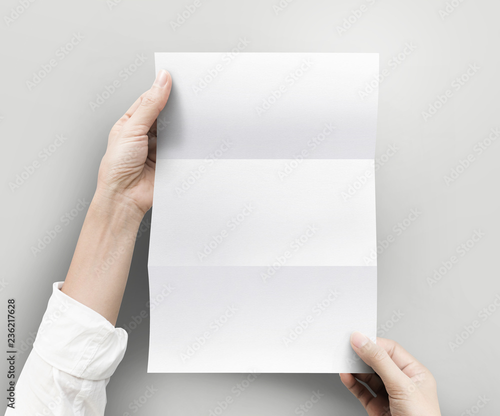 Hand holding empty white blank paper sheet A4 size on grey background ...