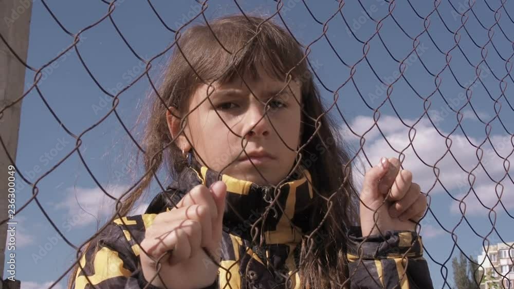 Sad child behind the fence. Child abuse. Child in a cage. A sad little ...