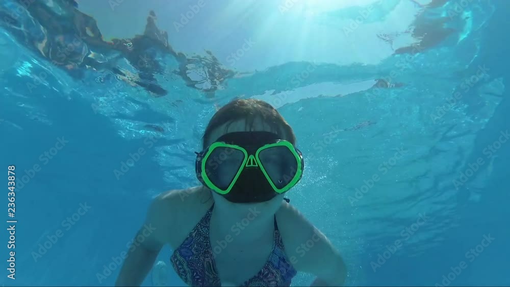 happy girl with a mask in a swimming pool underwater swims takes the ...