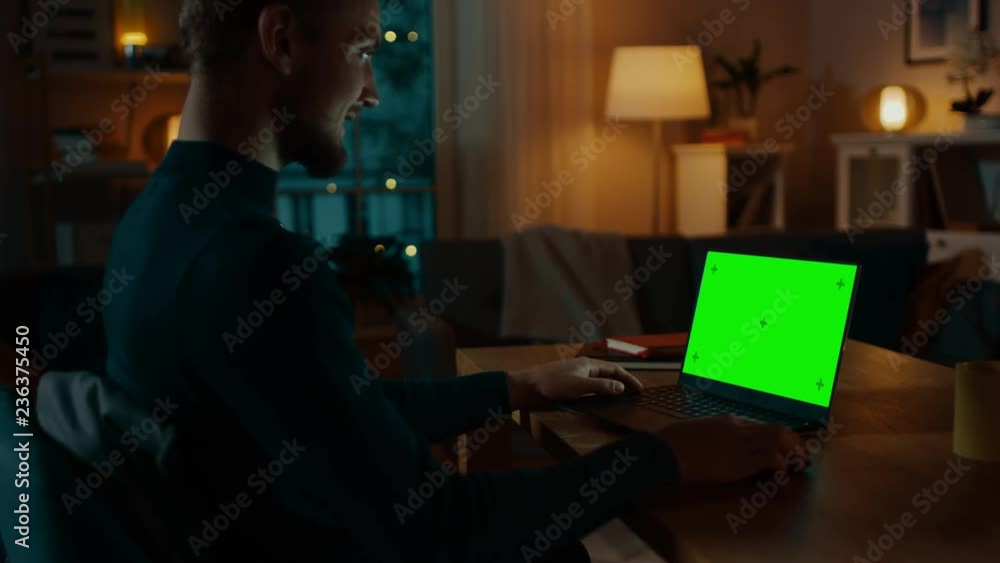 Man Sitting at His Desk Works on a Laptop with Green Mock-up Screen ...