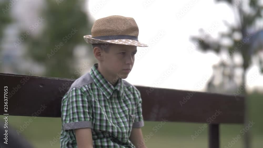 unhappy suspicious boy sitting on a bench in the park, a boy with a bad ...