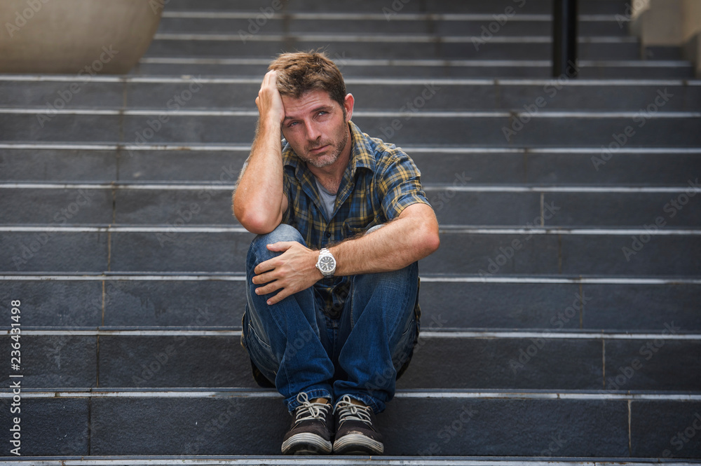 young sad and desperate man sitting outdoors at street stairs suffering ...
