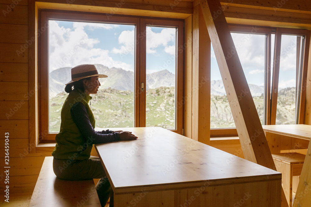 Young beautiful woman sitting near the window in shelter wooden hut and ...