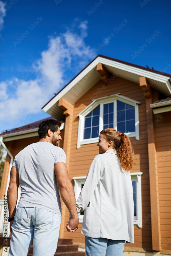 Back view of new owners of house standing in front of it anad looking ...