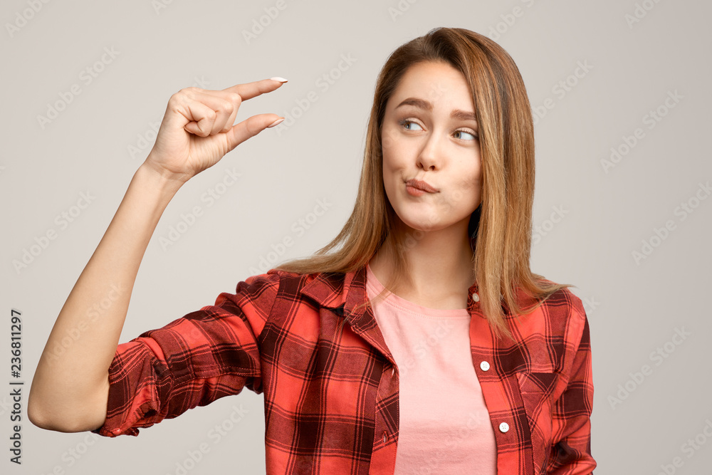 Positive woman with stylish hairdo, shows something very tiny or small ...