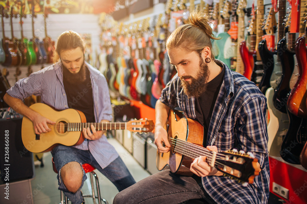 Two concentrated young man playing on acoustic guitars. They sit on ...