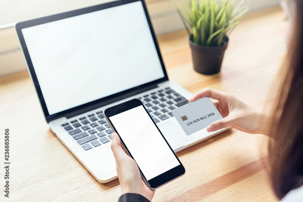 woman holding smartphone and using laptop on table in office room on ...
