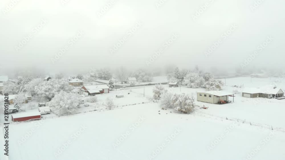 Aerial-Flying by snowy fields and a rural small town main street with ...