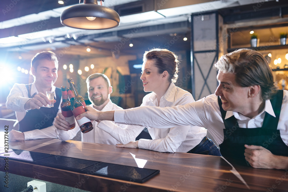Happy excited young restaurant colleagues reaching hands with beers to ...