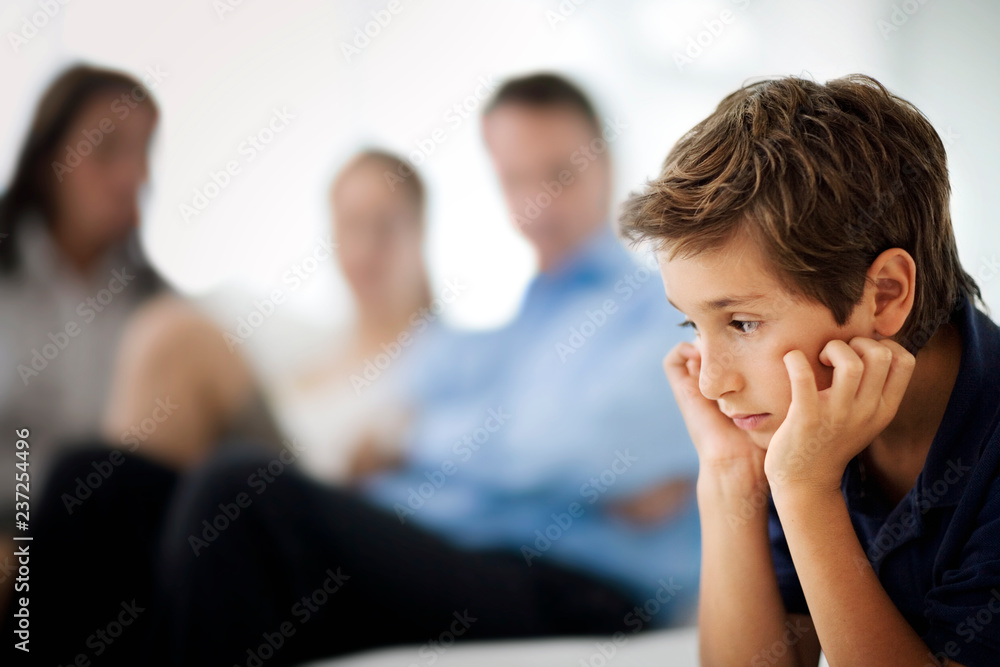 Boy sitting apart from his family on a sofa. Stock Photo | Adobe Stock