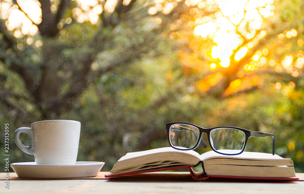 A cup of coffee and glasses on book on the wooden table with morning ...