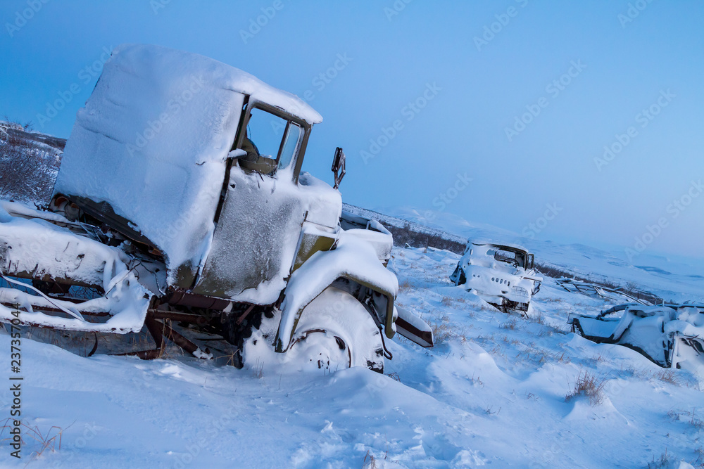 Old broken truck and cars in a dump in the tundra among the snow ...