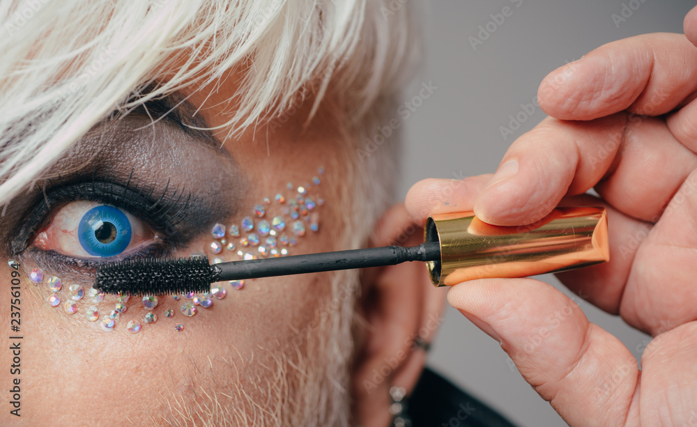 Final touch. Fashion male eye makeup. Transgender man apply mascara ...