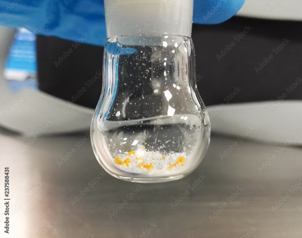 Weighing chemical reagents (white and yellow powders) into a glass ...