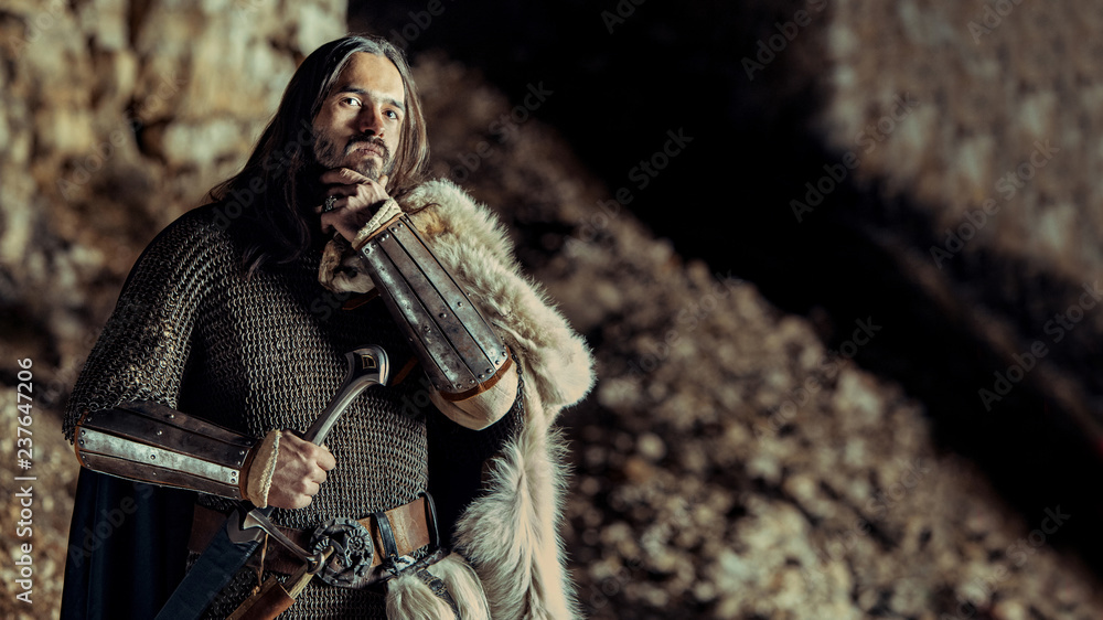 Long haired knight with the two-handed sword. Rocks on the background ...
