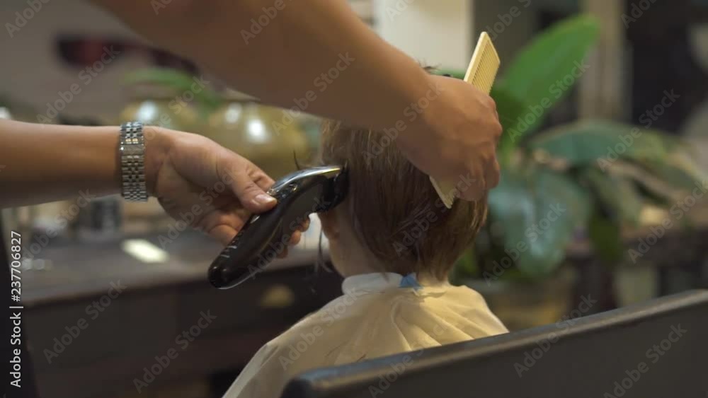 Cutting children hair with electric razor in barbershop. Closeup kids ...
