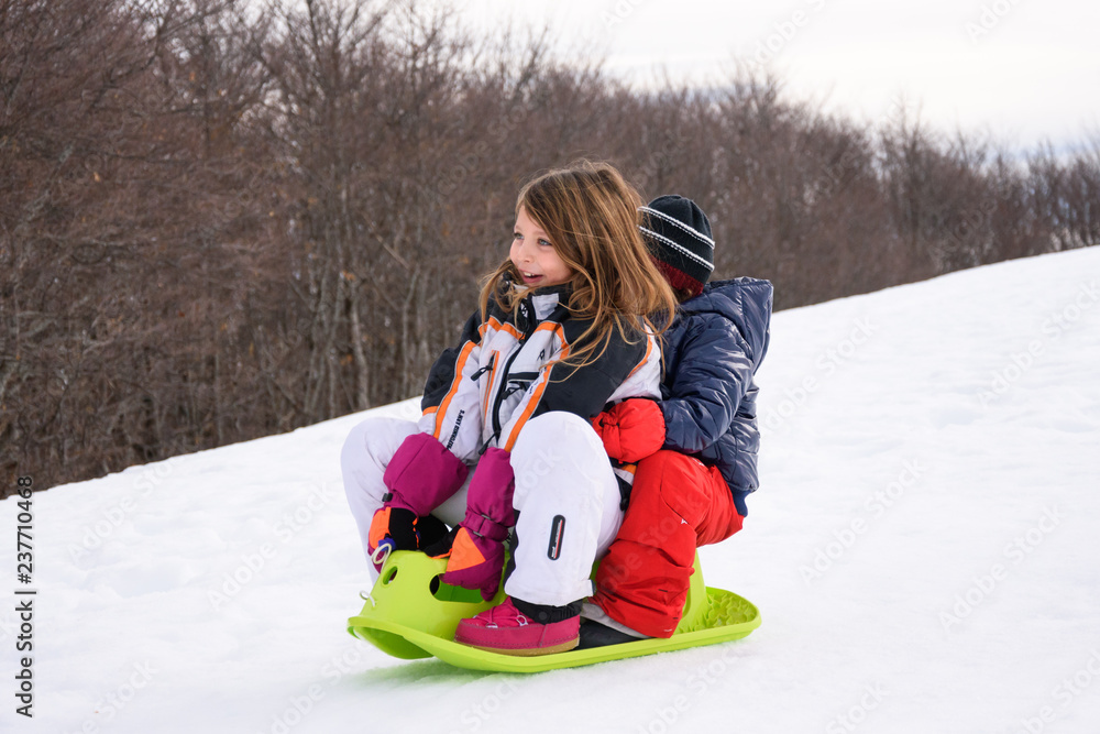 Two children sledding, playing together on snow with slider and ...
