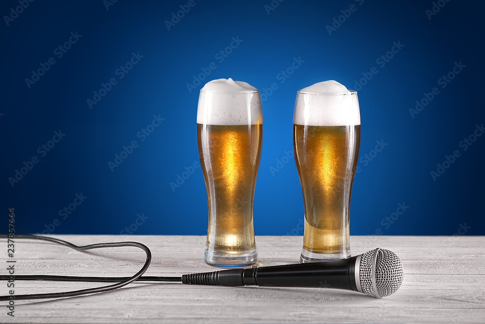 Two glass beer and microphone on white wooden desk. Blue background ...