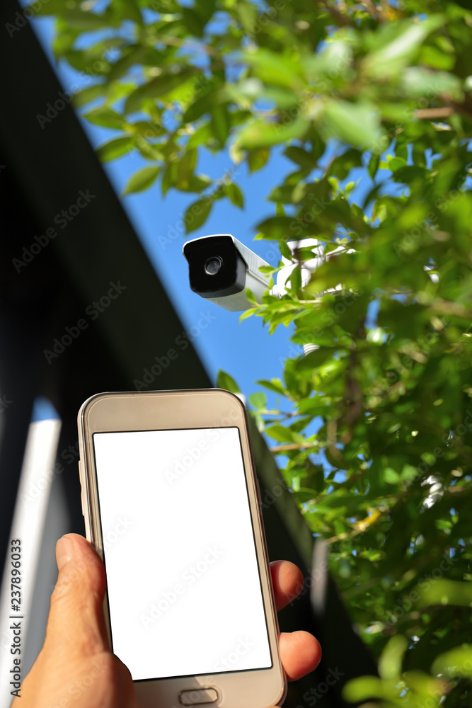 A modern white security CCTV camera on a house gate wall, surrounded by ...