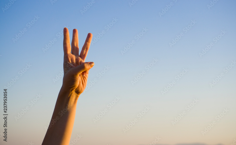 Hand doing / showing number three gesture symbol on blue summer sky ...