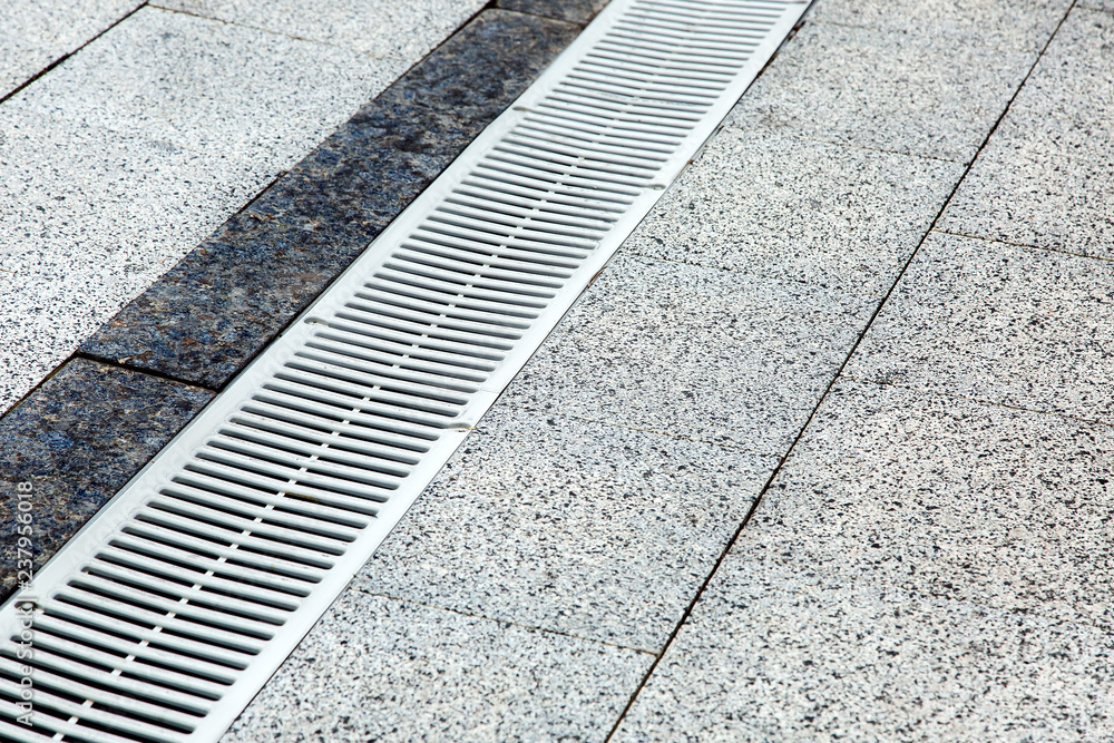 pedestrian pavement paved with stone tiles with metal drainage lattice ...