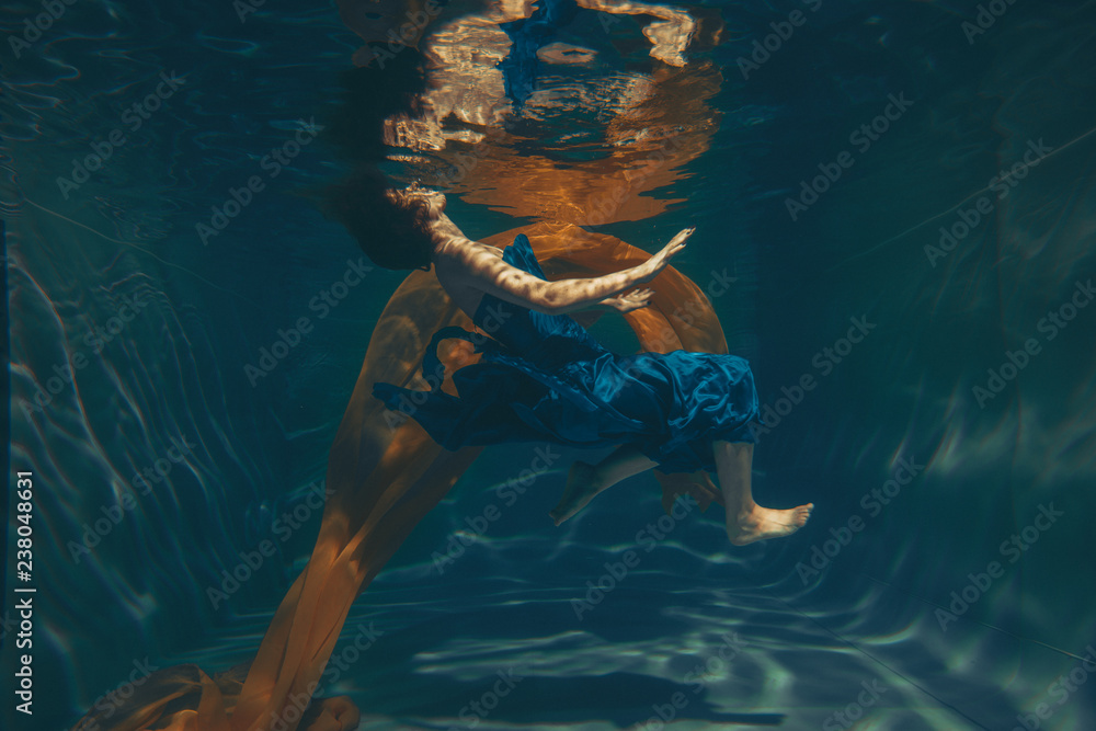 cute sporty female swims underwater as a free diver in a blue evening ...