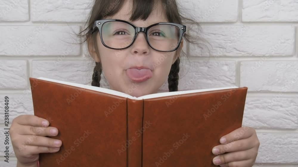 Sticking out tongue. A cute little girl in glasses with a book shows ...