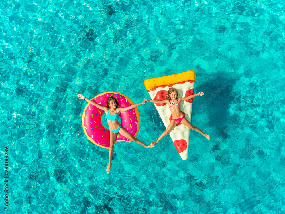 Aerial view of two young girls floating in sea on inflatables holding ...
