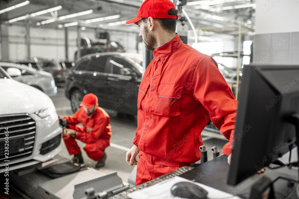Two handsome auto mechanics in red uniform making wheel alignment with ...