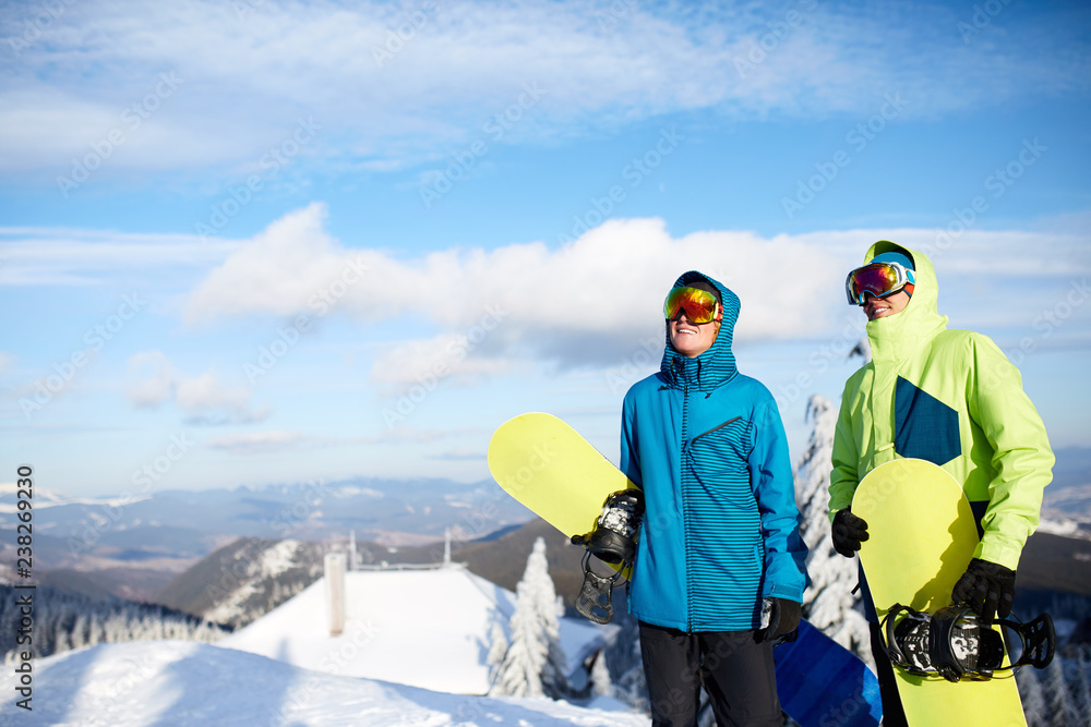 Two snowboarders posing at ski resort. Riders friends carrying their ...