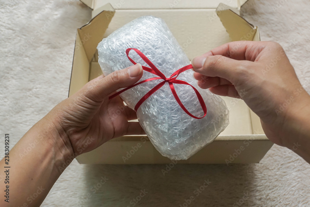 close up woman hand tie a red ribbon on gift wrapped with bubble sheet ...