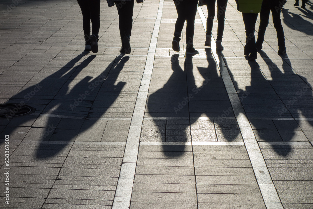 Silhouettes and shadows of people walking along a city street. Contrast ...
