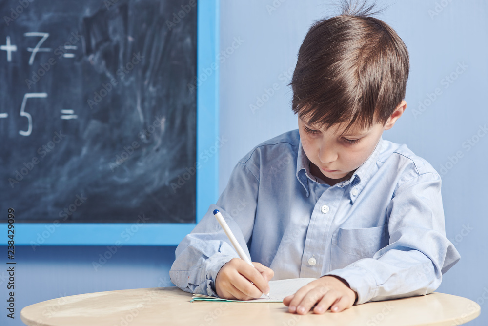 Caucasian schoolboy in uniform carefully doing task at home. First time ...