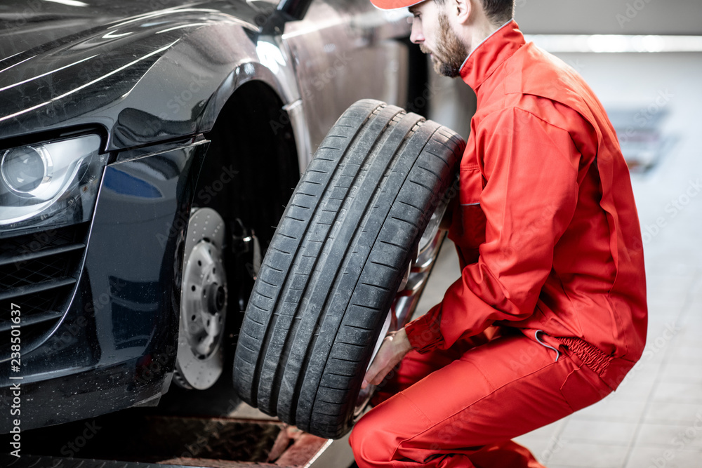 Car service worker in red uniform changing wheel of a sport car at the ...