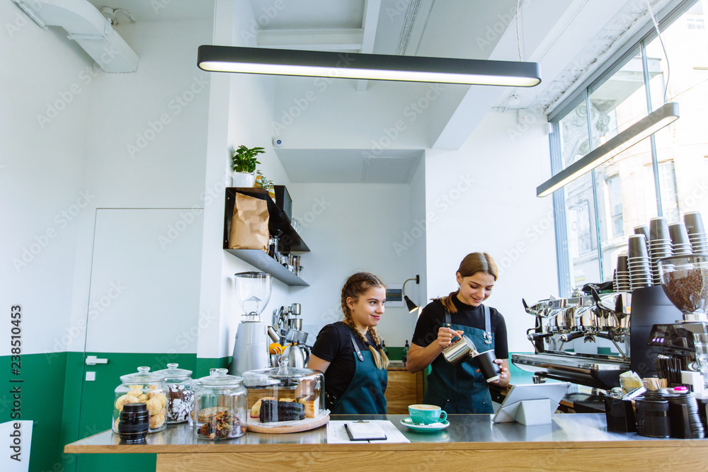 Two positive smiling female barista working together behind counter ...