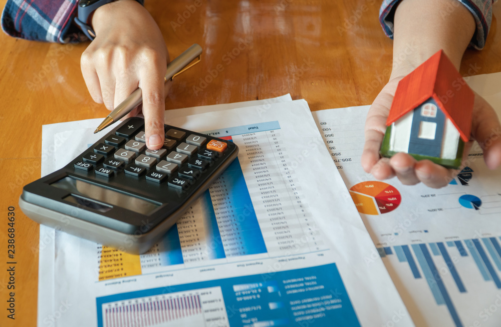 Woman holding house model in hand and calculating financial chart for ...