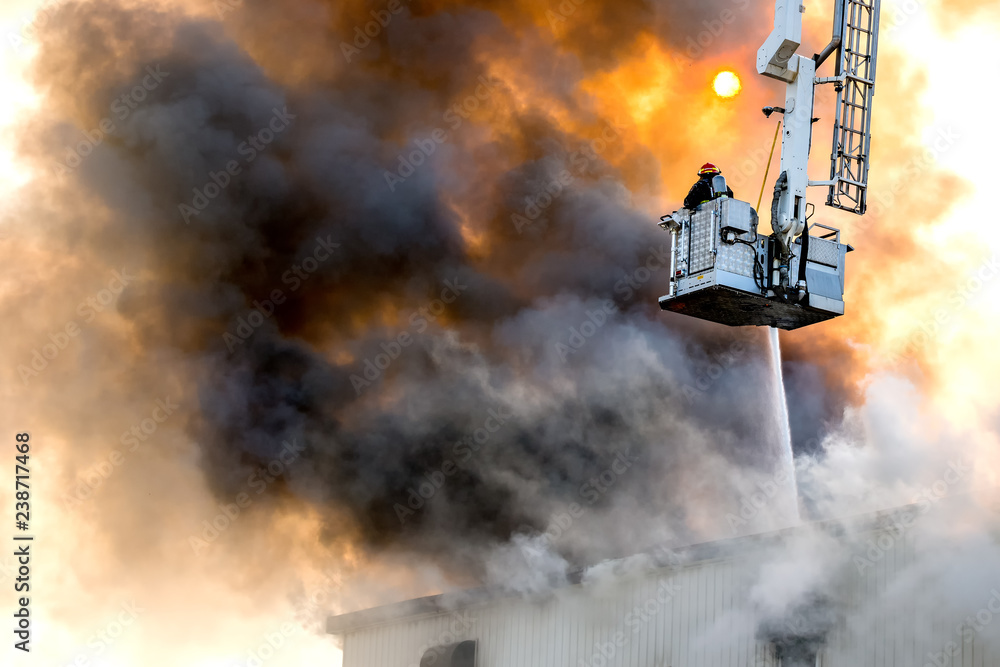 Unidentifiable fireman fighting a fire from bucket above building. A ...