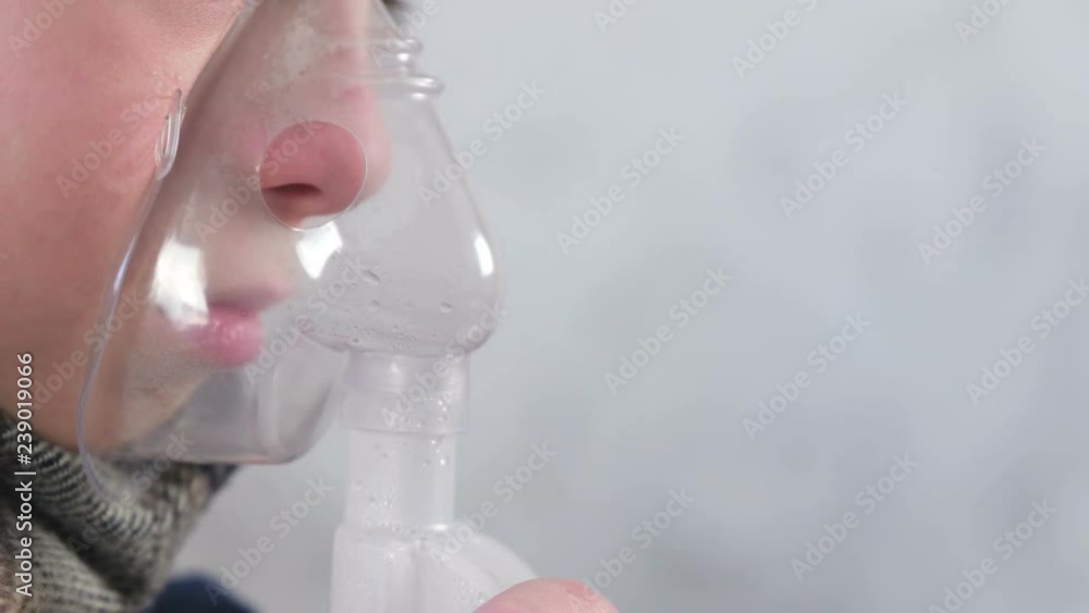 Sick boy inhaling through inhaler mask, nose and lips close-up side ...