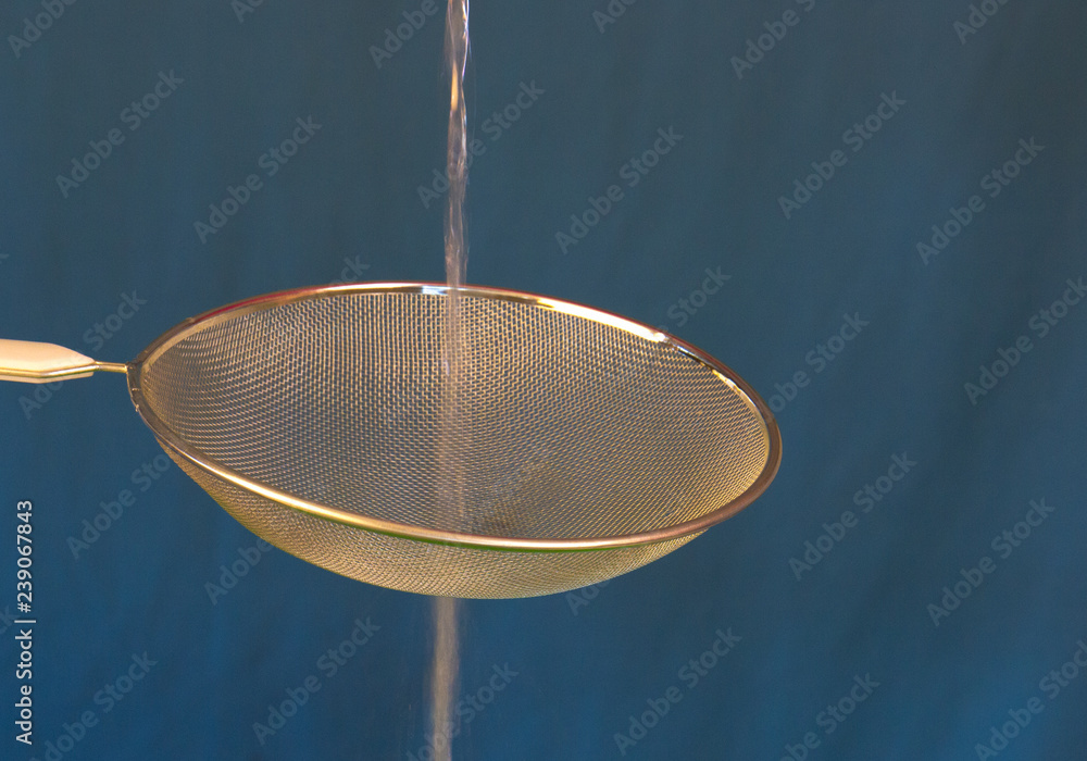 A stream of water pouring through a sieve isolated against a clear ...