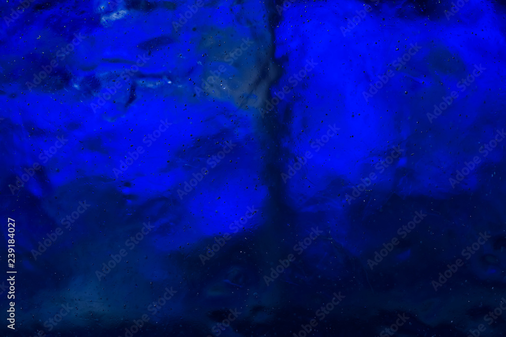Clear transparent ice with small bubbles illuminated with blue light ...