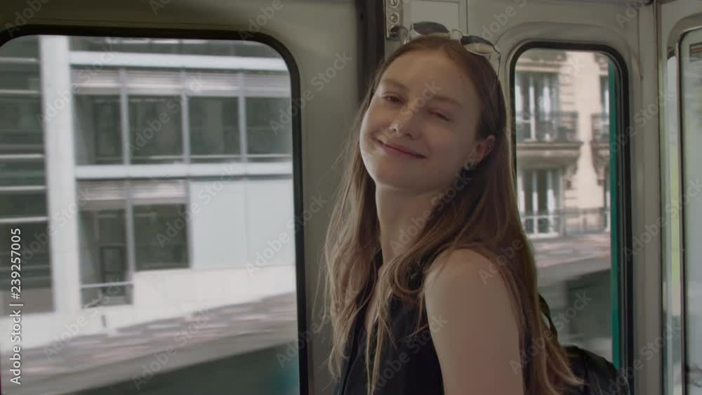 Cute woman riding a train turns and looks at the camera, makes a face ...